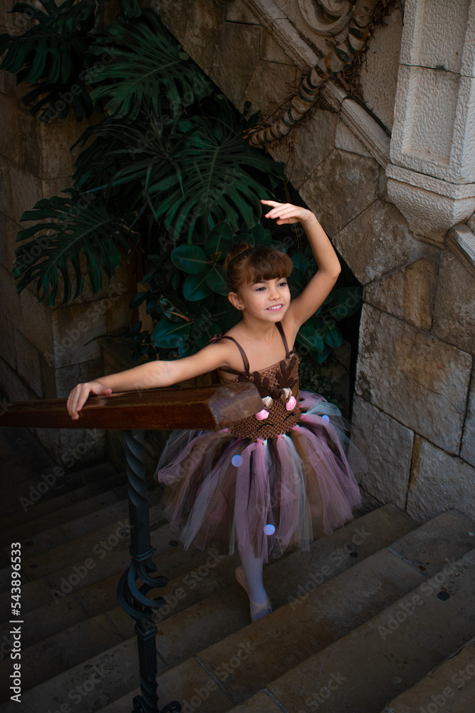 Niña pequeña bailando ballet en un jardín con muros románicos de piedra ...