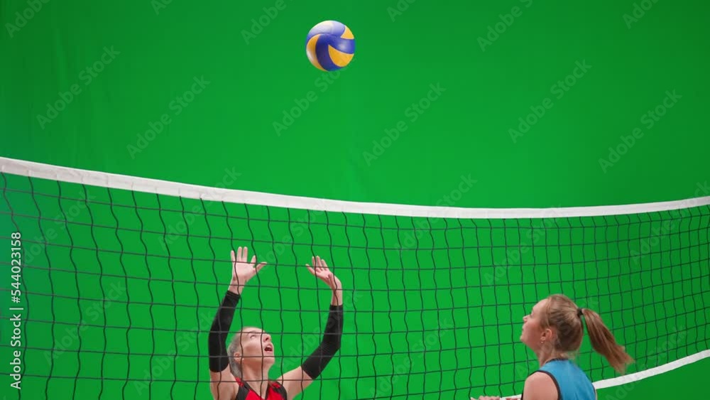 Two young women in blue and red uniforms playing volleyball on green ...