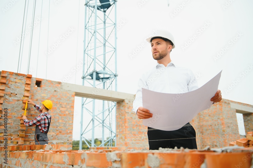 Architect at a construction site with blueprints. Stock Photo | Adobe Stock