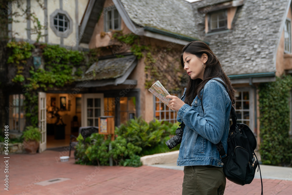 asian Chinese lady solo traveler reading a guide map near an ivy covered cottage style hotel ...