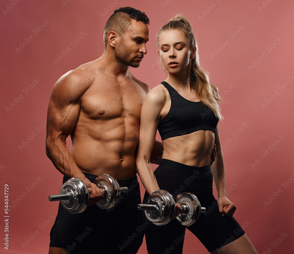 Fitness male and female models with equipment at pink background. Sporty couple with dumbbells ...