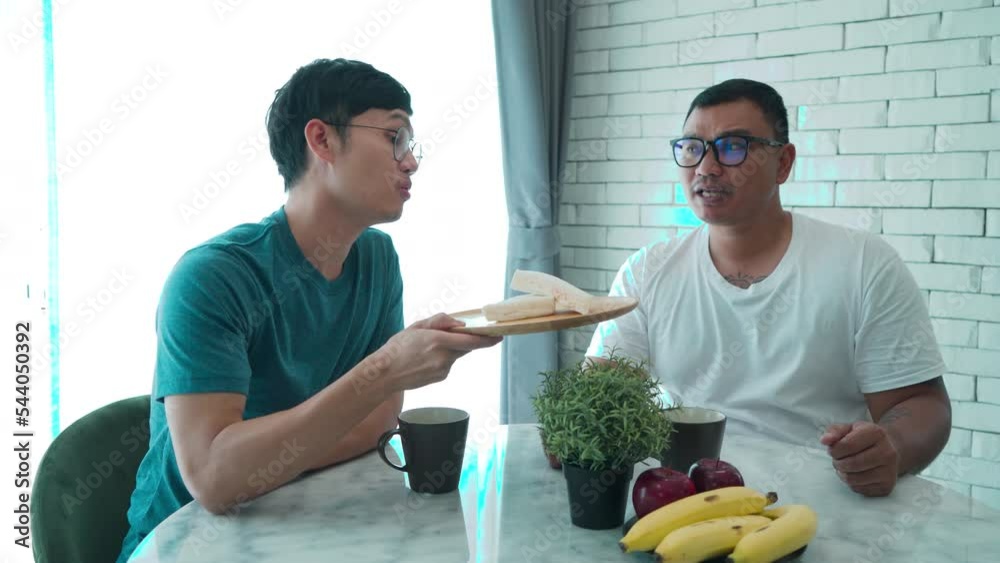 GAY couple having breakfast sandwiches and coffe together in kitchen ...