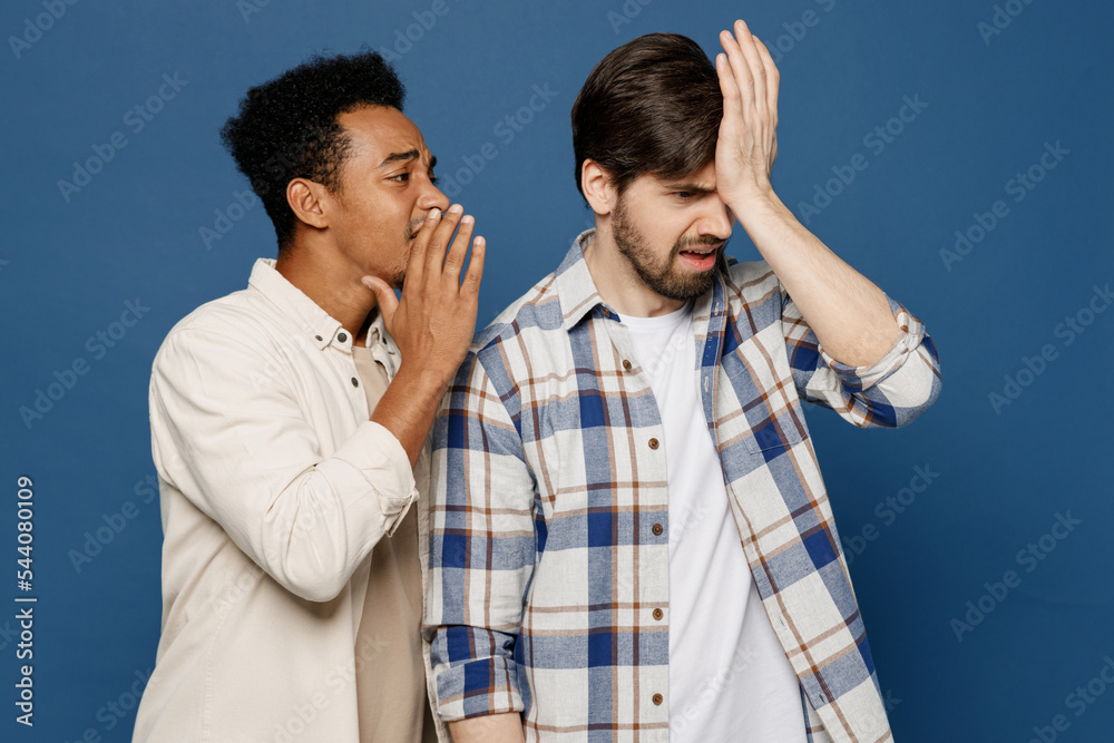 Young two friends shocked sad men wear white shirts together whisper gossip and tells secret ...