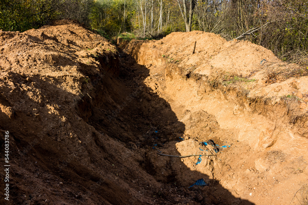 A deep trench dug in sandy soil in a forest area for laying engineering ...