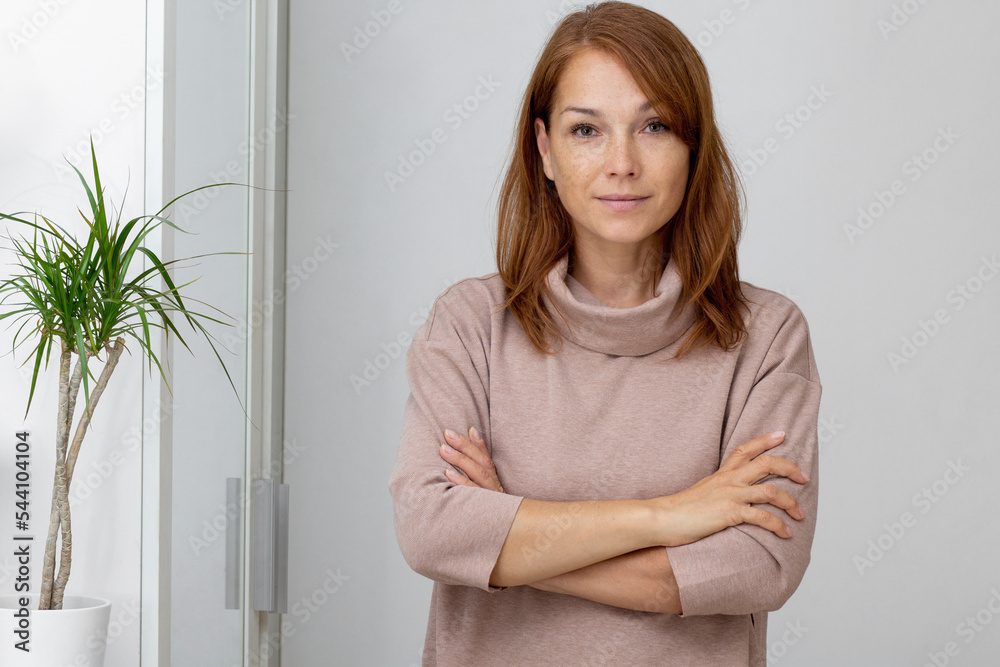 Waist up beautiful smiling middle aged woman holding crossed hands on breast looking at camera ...