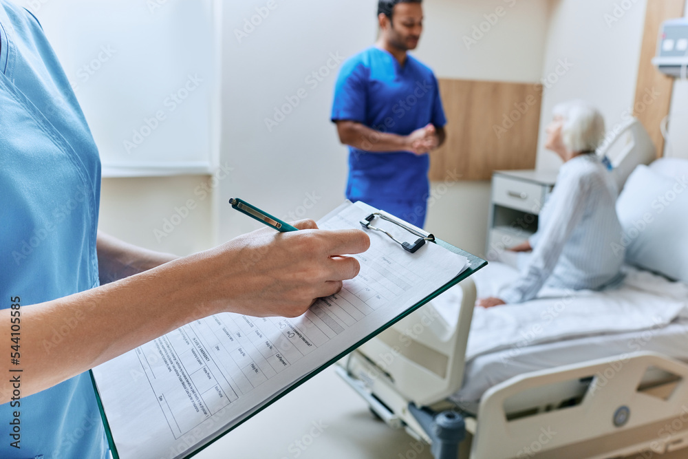 Nurse takes notes in medical chart in hospital room with elderly ...