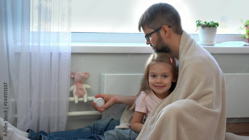 Family, father and child sit in plaid near heating radiator and adjust ...