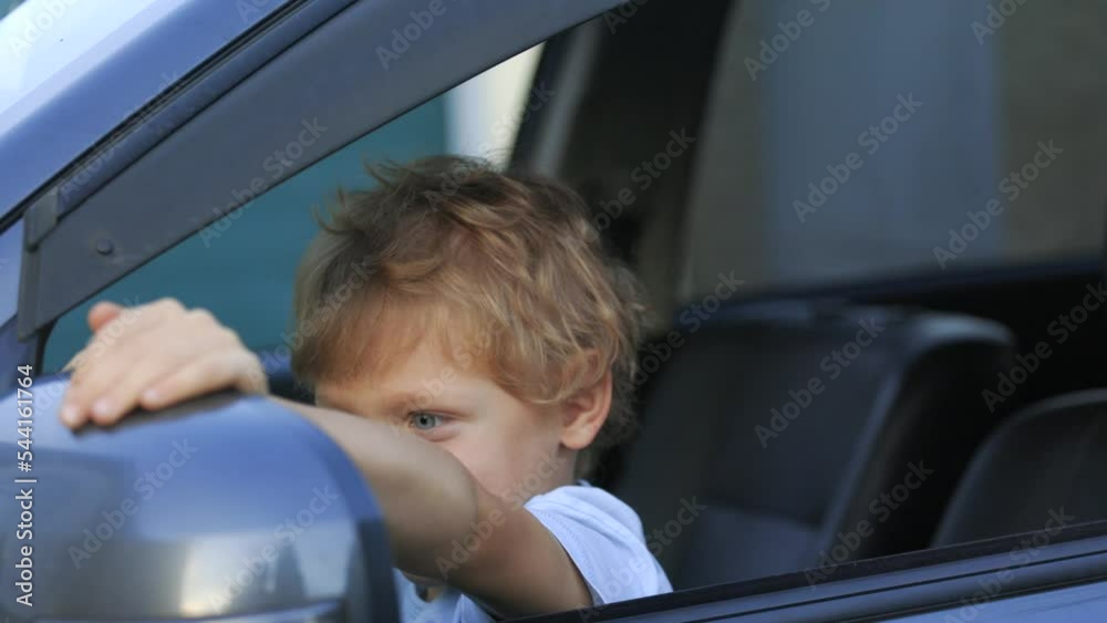 Boy sits in black interior of car, touching the side mirror with his ...