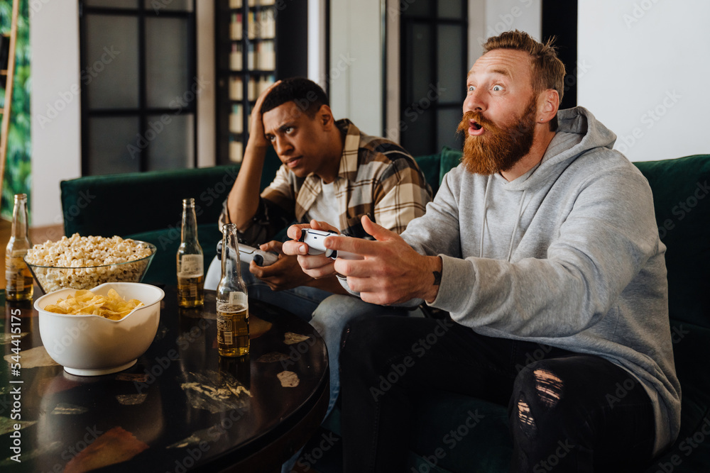 Excited white ginger man playing video game with his friend and winning ...