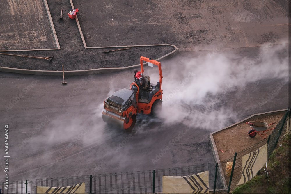 Orange asphalt paver machine laying asphalt road in the rainy day and ...