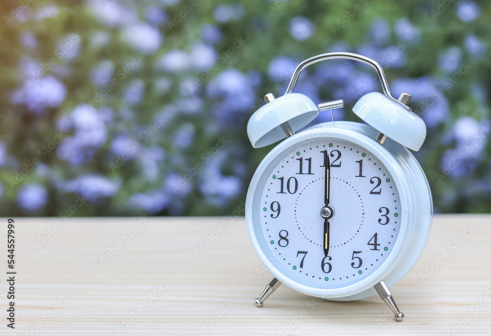 Front view of white vintage alarm clock showing 6 o clock on the table ...