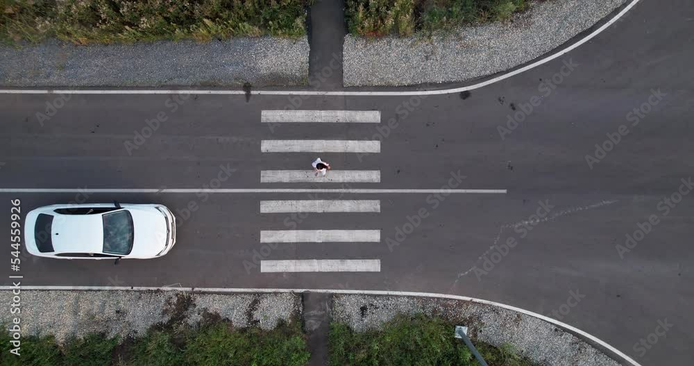 A car gives way to a person at a pedestrian crossing. A white car stops ...