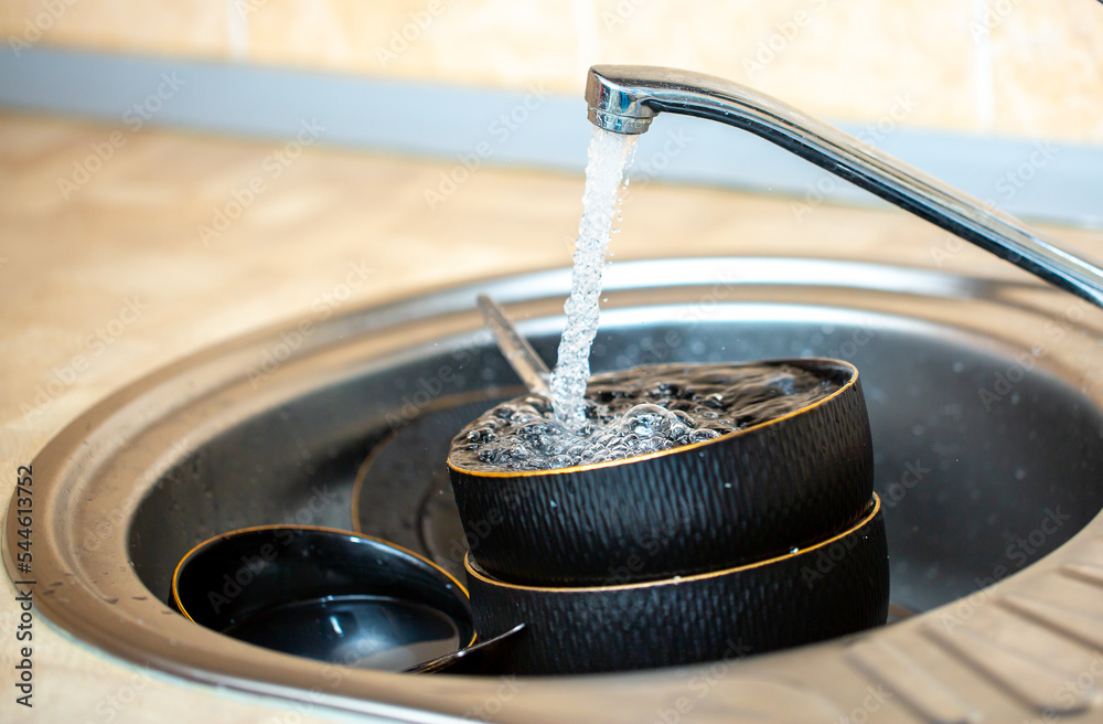 A pile of dirty dishes in the sink. Black dishes are stacked in a metal ...