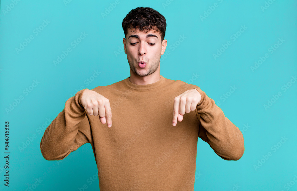 with open mouth pointing downwards with both hands, looking shocked ...