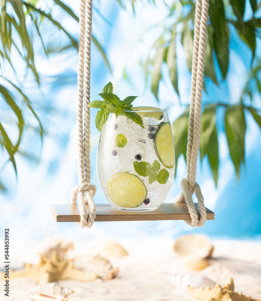 Classic gin tonic on a swing on a sandy beach surrounded by palm trees ...