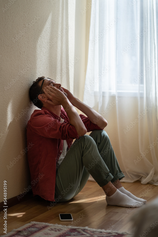 Upset depressed young man sitting with closed eyes on floor at home ...
