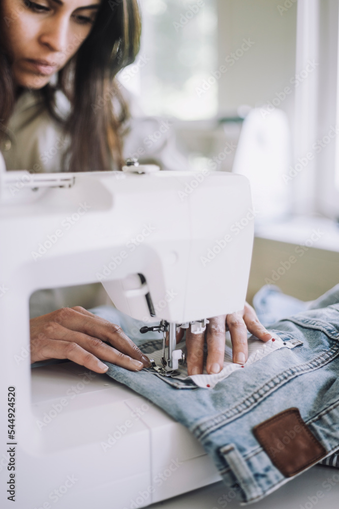 Female fashion designer sewing fabric on jeans pocket using sewing ...
