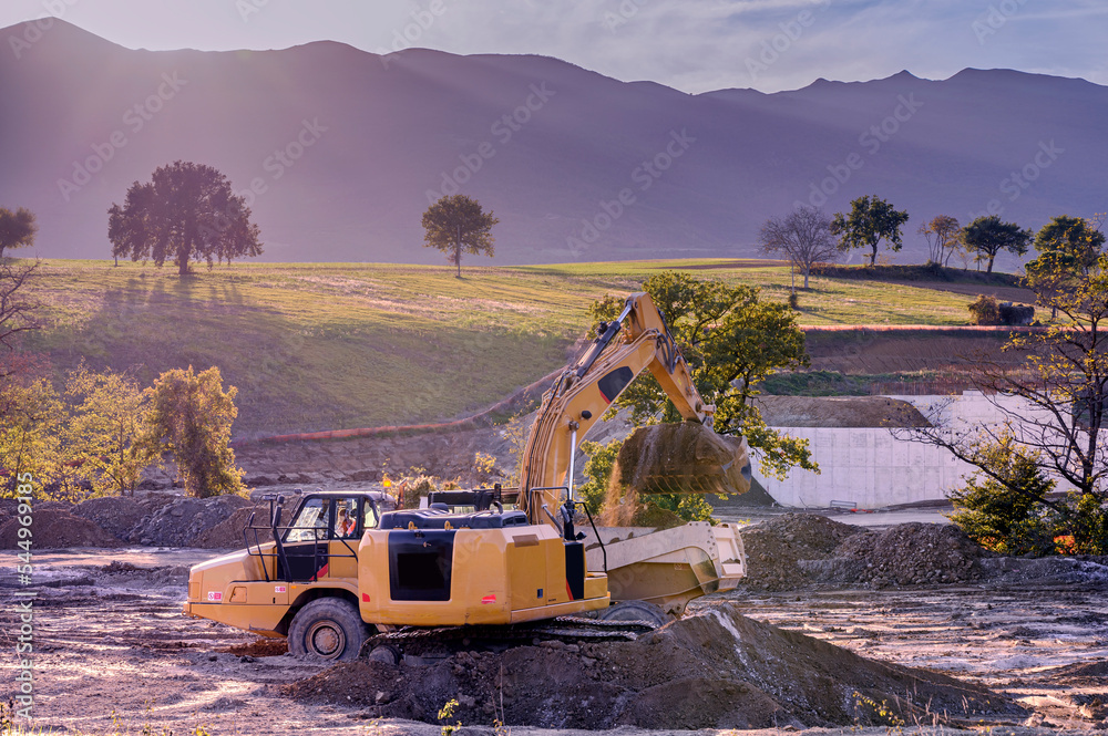 Excavator with bucket moves filler earth on a Articulated dump trucks ...