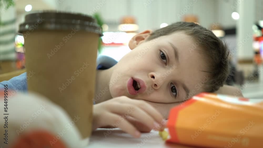 tired boy put his head on the table at the food court and eats french ...