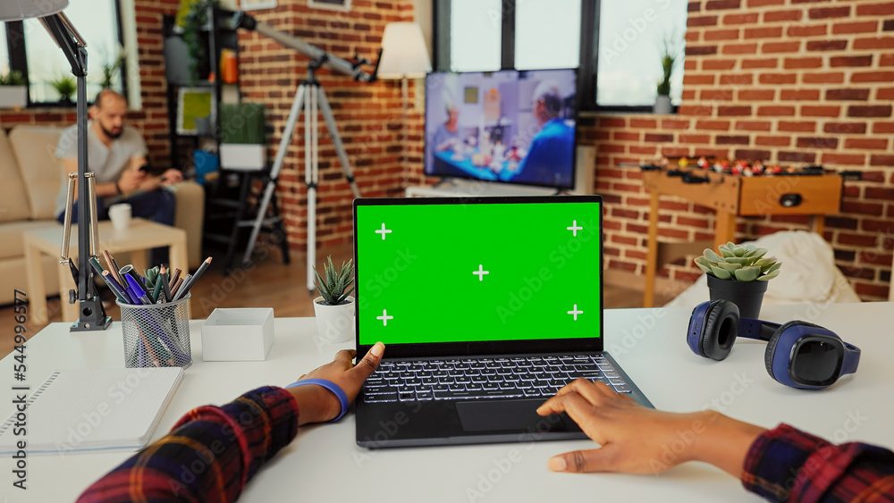Young adult working on laptop with isolated green screen on display ...