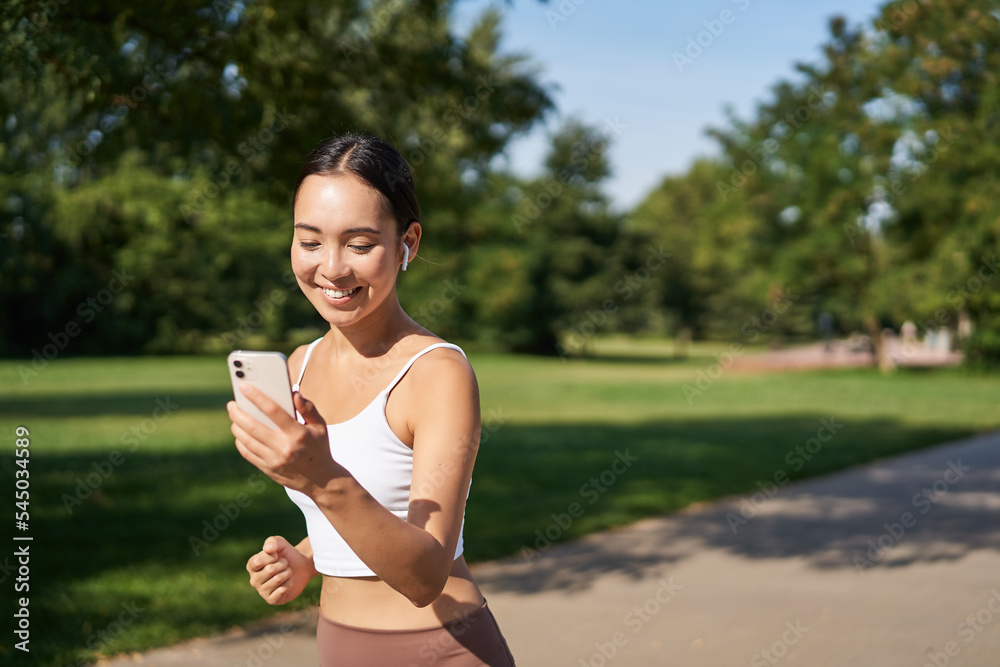 Happy asian fitness girl running and checking her stats, daily goals on smartphone app. Young ...