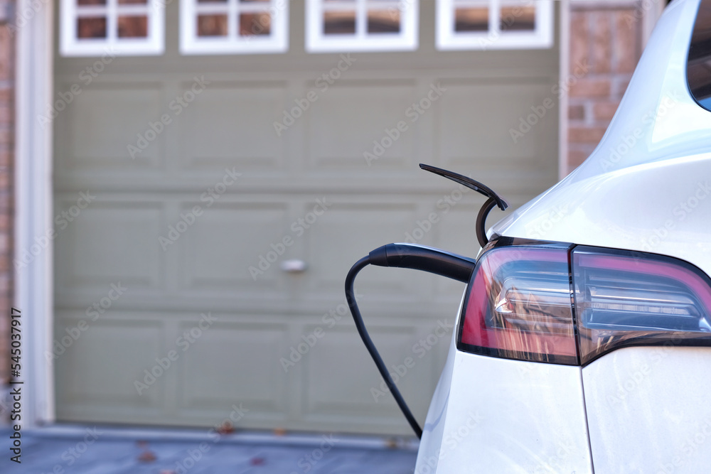 Foto de Back view of white EV car charging on driveway in front of ...