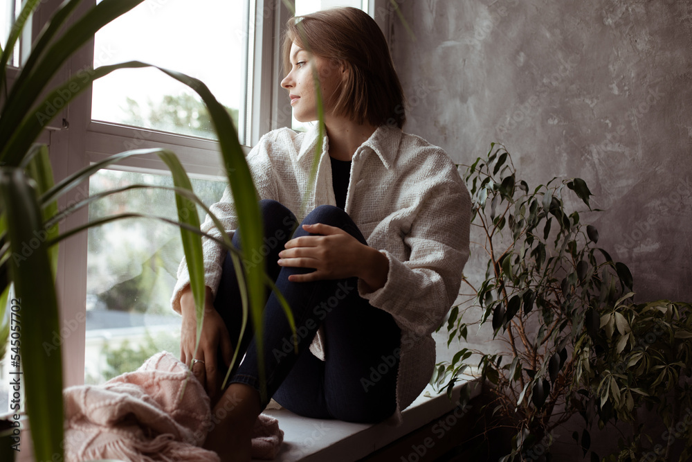 Calm, thoughtful romantic young woman looking out window, sit on ...