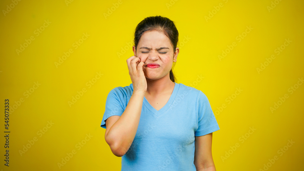 Young woman scratching face or cheek, isolated over yellow background ...