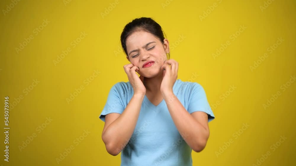 Young woman scratching face or cheek, isolated over yellow background ...