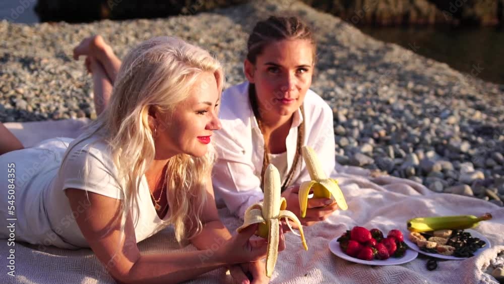 Two woman eating banana on the beach at sunset time. Girl Hand Holding ...