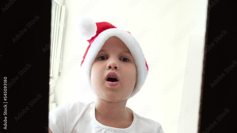 Little kid girl in Santa helper hat opens box with present. Xmas ...
