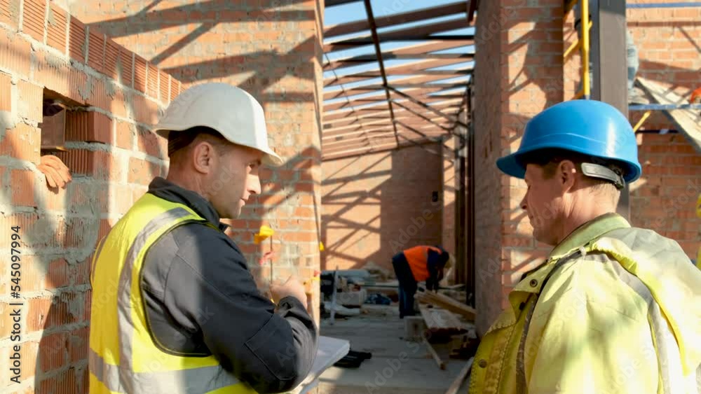 Two builders walking forward on the roof of construction site. Builder ...