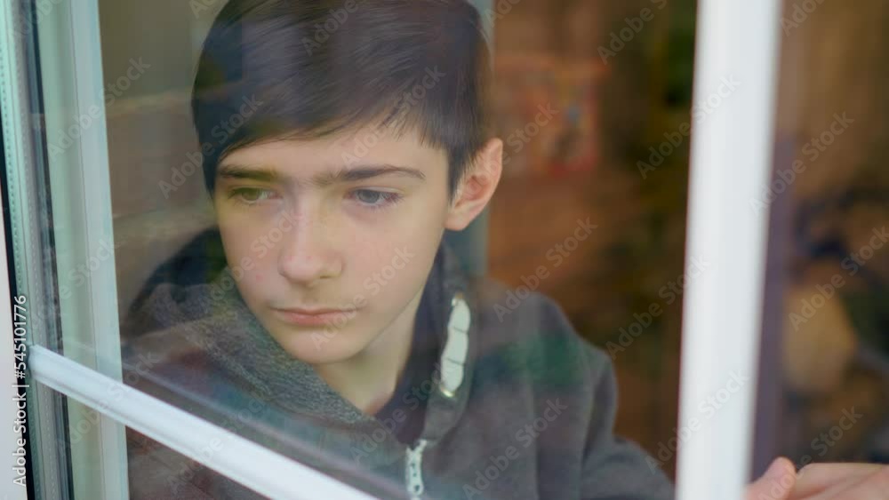Sad boy looking through window from room. Unhappy face of schoolboy ...