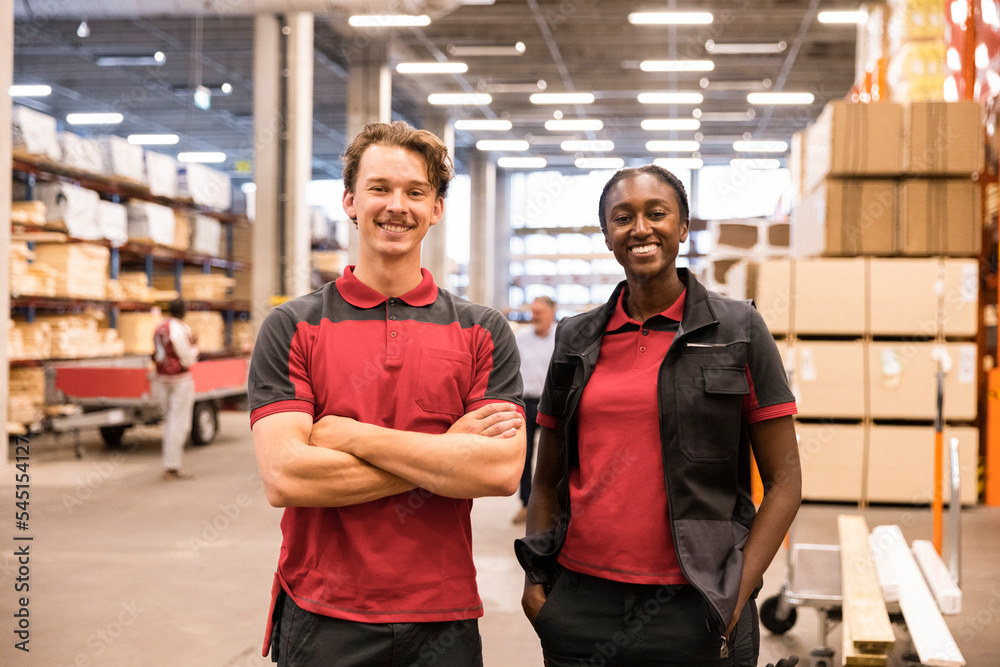 Portrait of smiling salesman with arms crossed standing with female ...
