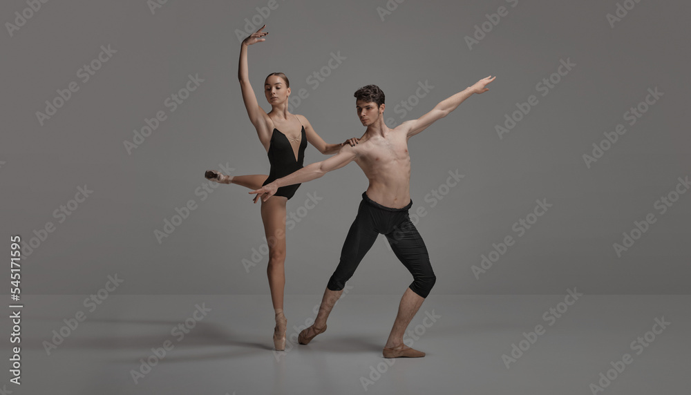 Young man and woman, ballet dancers performing isolated over dark grey ...