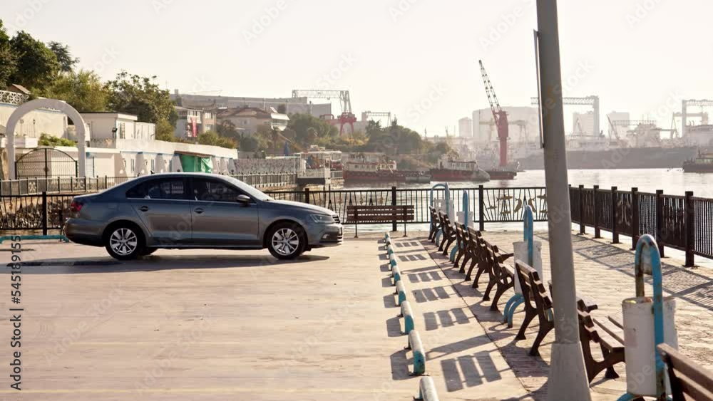 lonely gray car is parked on waterfront in parking lot with port and ...