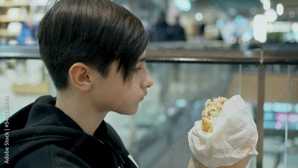 Boy in fast food cafe eats burger. Portrait of hungry teenager ...