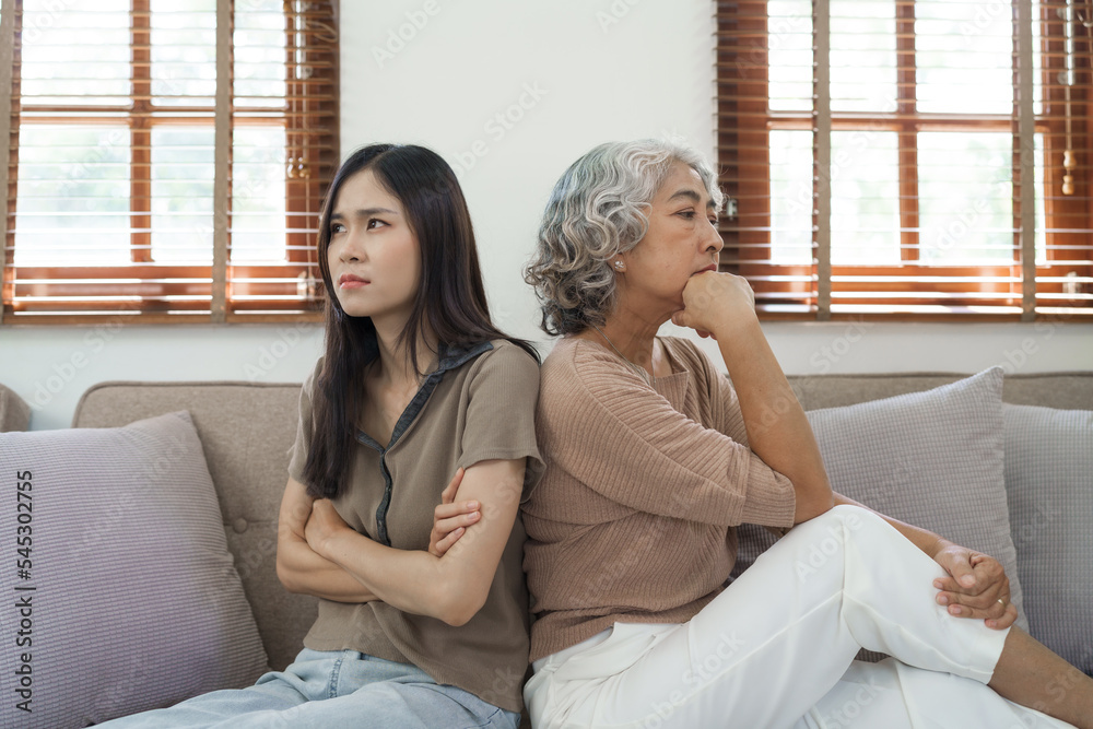 Elderly mother and grown up daughter sit on couch separately, Close up angry strict mother ...