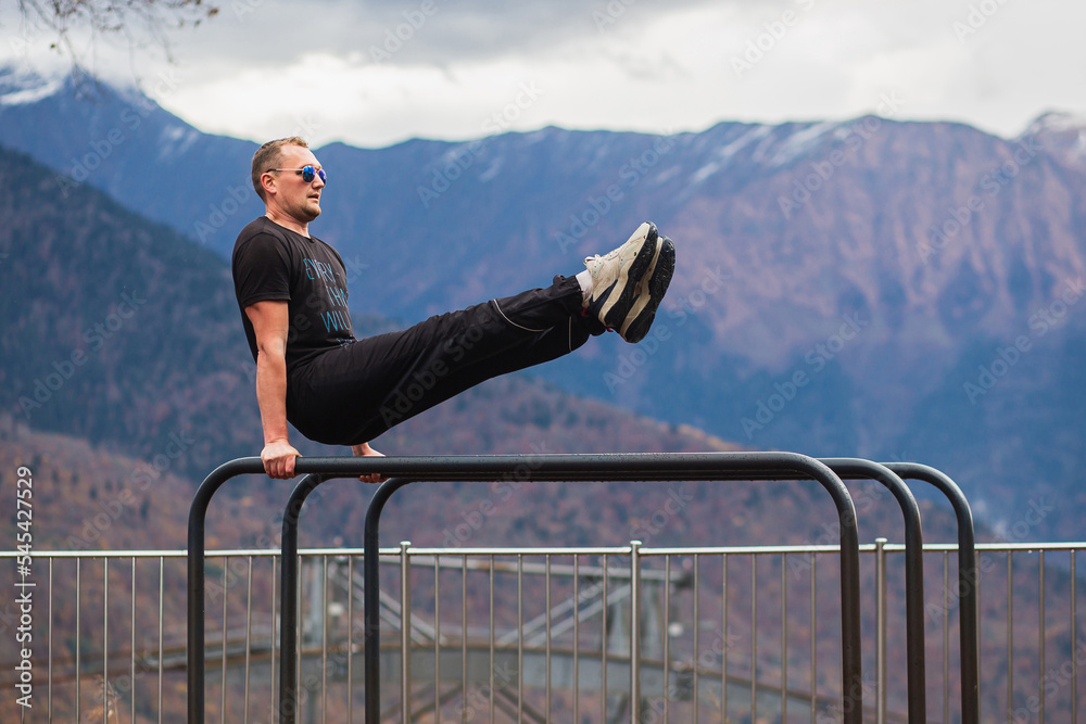 Foto de Strong man pumps abdominal muscles on uneven bars, rear view ...