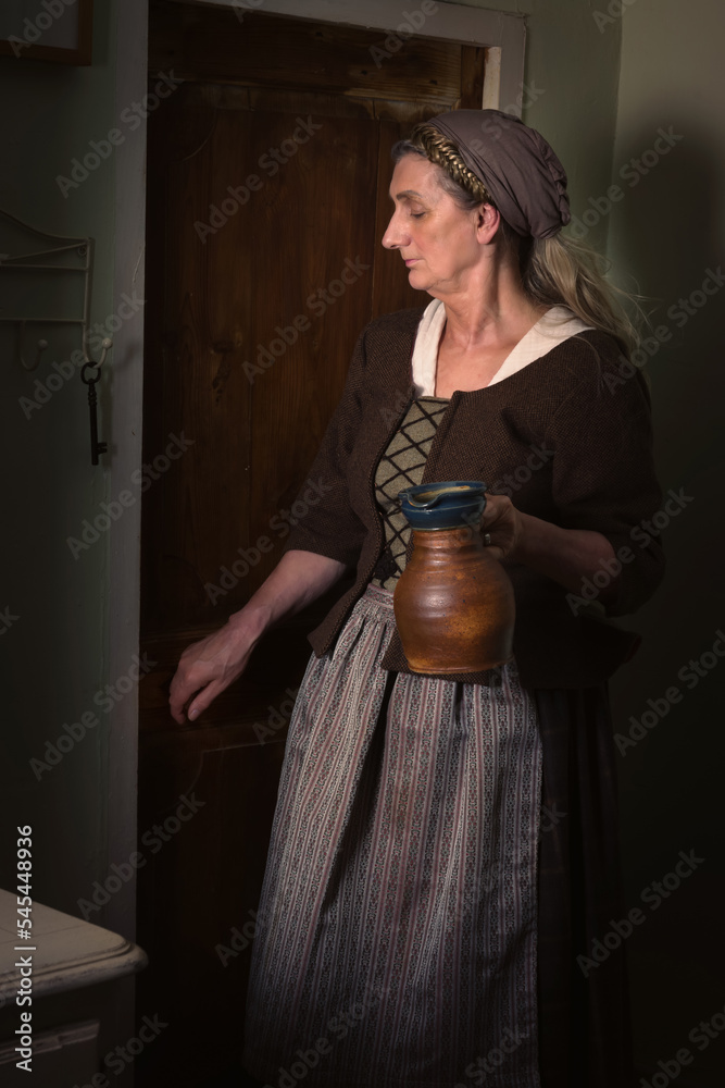 Lady in medieval peasant outfit entering a room with a stone jug in her ...