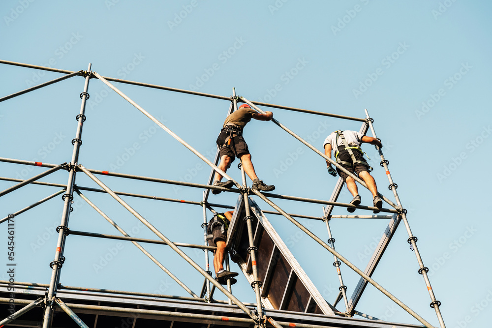 Builders mount a concert stage. Workers build a metal structure to ...