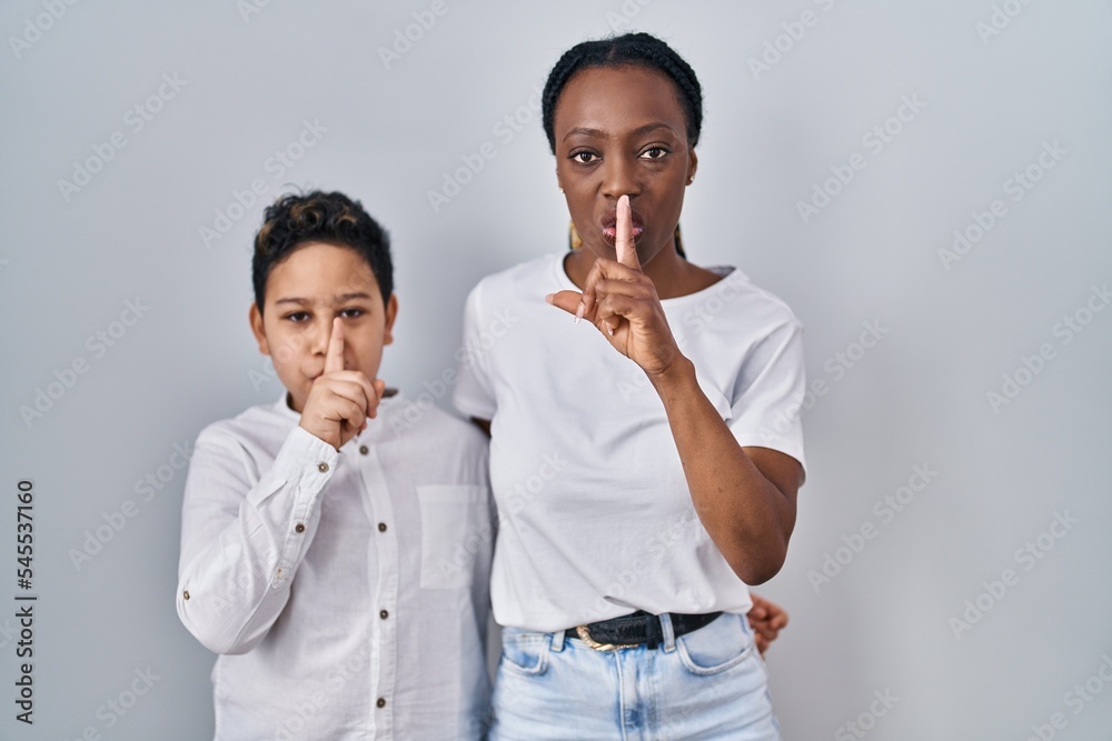 Young mother and son standing together over white background asking to ...