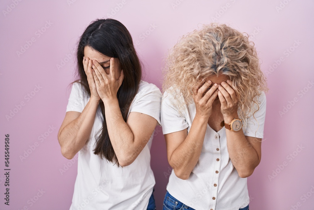 Mother and daughter standing together over pink background with sad ...