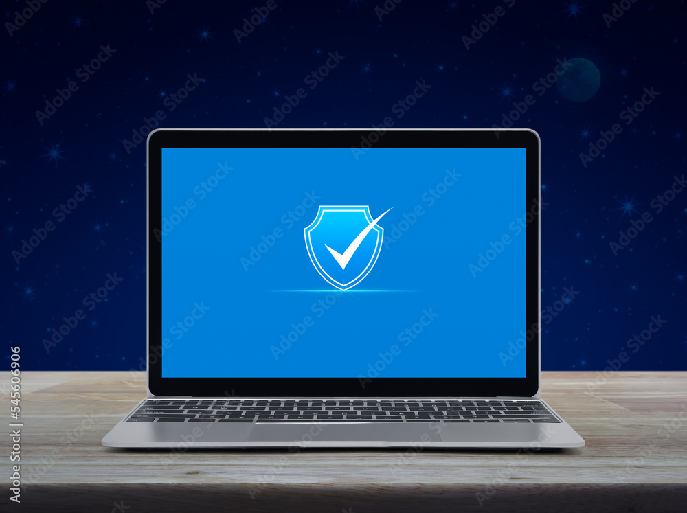 Security shield with check mark icon on modern laptop computer monitor screen on wooden table ...