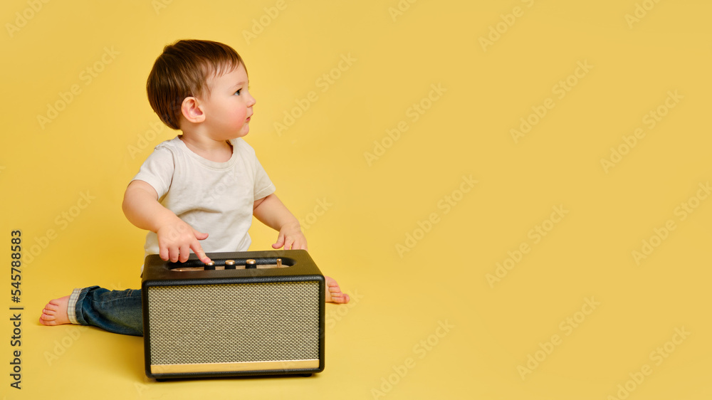 Toddler baby plays with a wireless music speaker on a studio yellow ...