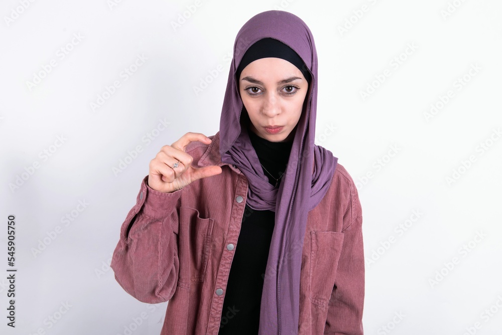 Displeased young beautiful muslim woman wearing hijab against white ...