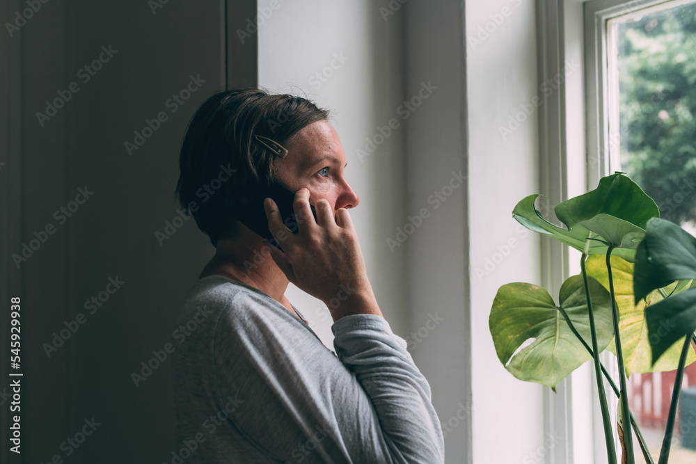Sad alone woman talking on mobile phone while looking out the window of ...