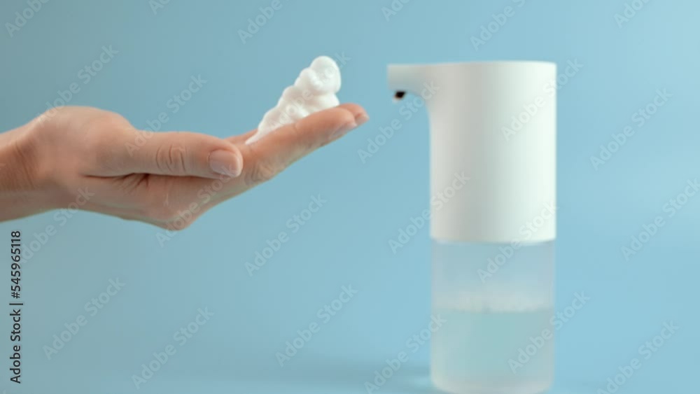 Using an automatic soap dispenser. Young girl woman brings her hands to ...