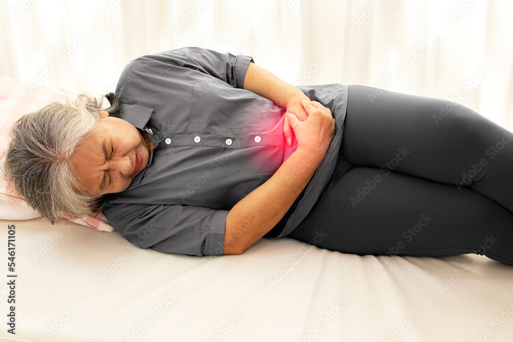 Asian elderly woman lying in bed uncomfortable with abdominal pain in ...