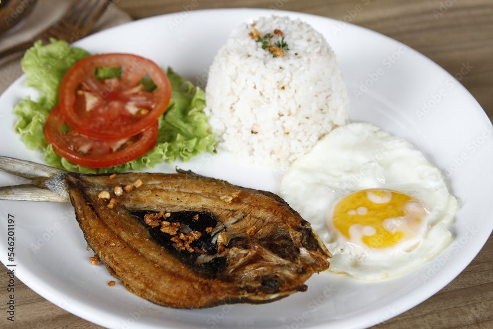 Filipino breakfast of fried bangus (milkfish) with garlic flakes and egg, lettuce, tomato and ...
